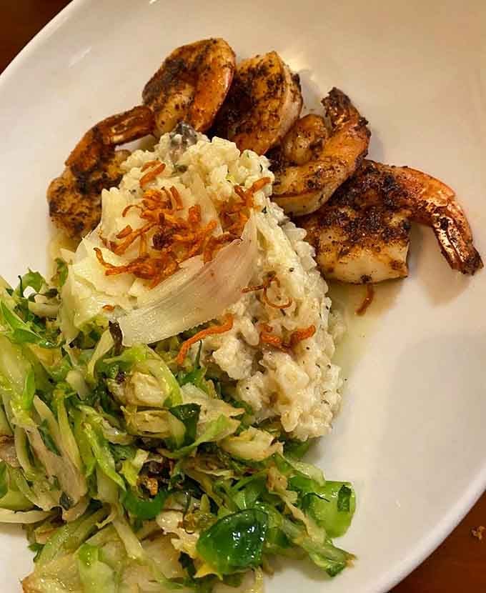 Blackened shrimp dance atop a creamy risotto island, surrounded by a sea of fresh vegetables—a vacation on a plate.