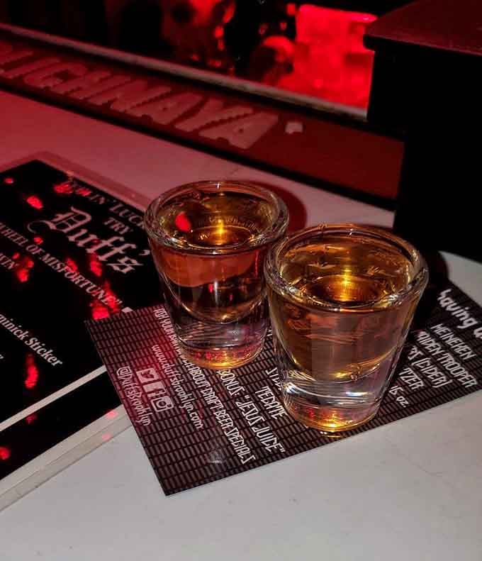 Shot glasses catch the crimson glow, promising liquid courage in this temple of excess.