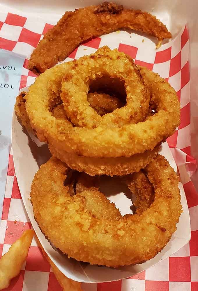 Onion rings stacked like edible train wheels, golden and crunchy enough to make you forget vegetables are technically involved.