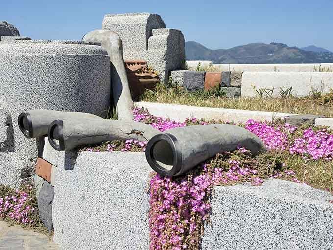 Purple blooms soften the granite edges, proving even experimental art installations appreciate a little natural decoration.