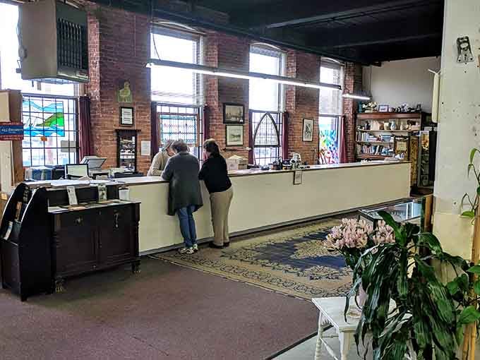 Natural light streams through tall windows at Acushnet River Antiques' welcoming counter, where treasure hunters begin their journey through history.