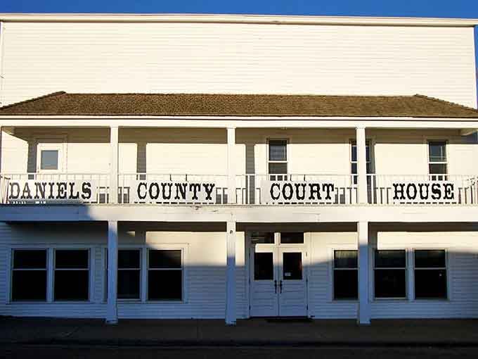 The Daniels County Courthouse gleams white against the Montana sky, a testament to small-town governance and prairie pragmatism.