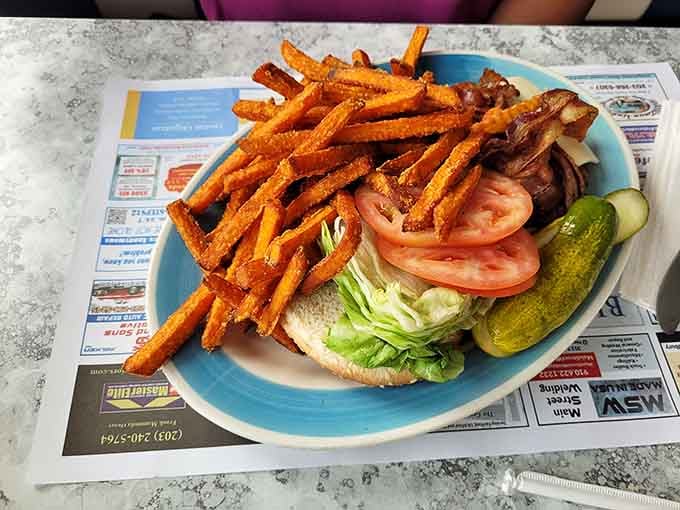Sweet potato fries piled high next to a burger that understands the assignment and then some, folks.