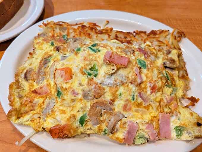 This omelet sprawls across the plate like it's claiming territory, loaded with enough fillings to make every bite an adventure.