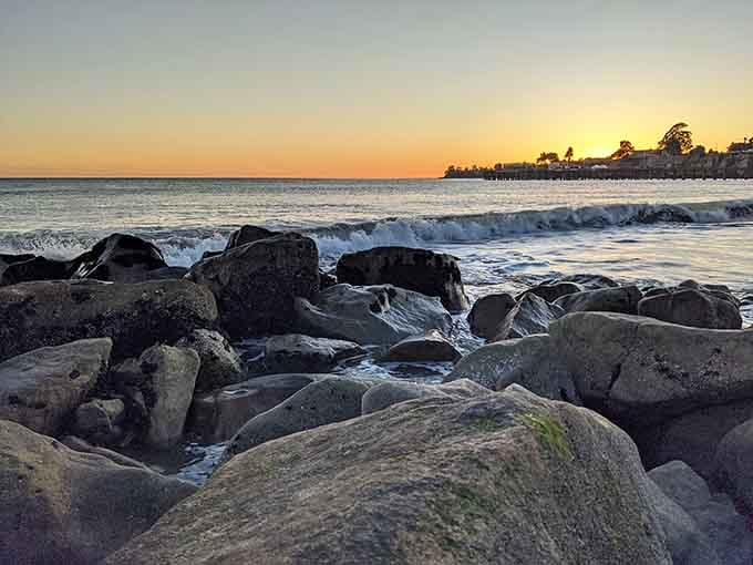 Sunset paints the rocky shoreline in golden hues while waves dance around ancient stones worn smooth.