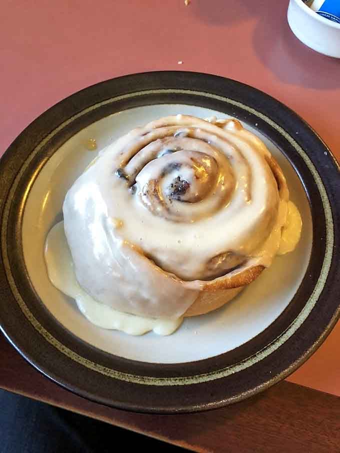The cinnamon roll arrives like a warm hug on a plate, frosting melting down its spirals in a sweet surrender that's worth every calorie.