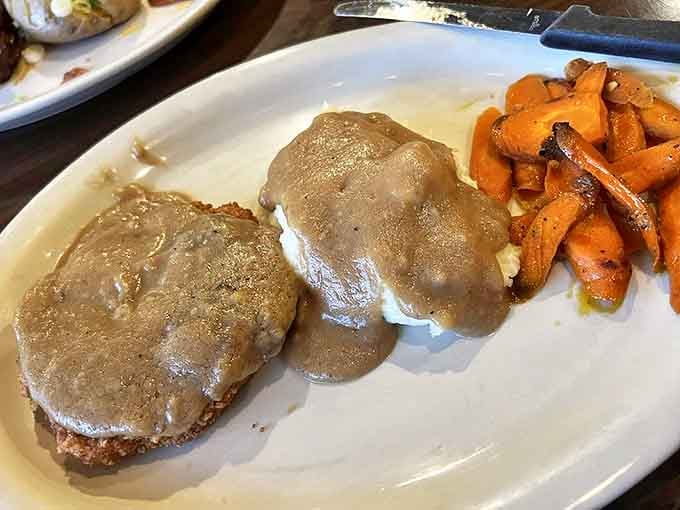 Country gravy cascades over what appears to be a hearty cutlet, accompanied by roasted carrots that look sweet enough to make even Bugs Bunny reconsider his raw vegetable stance.