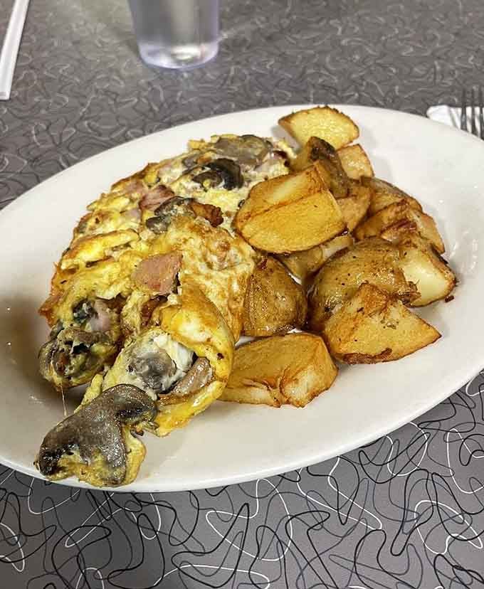 This omelet loaded with mushrooms and melted cheese alongside golden home fries defines breakfast perfection in every bite.