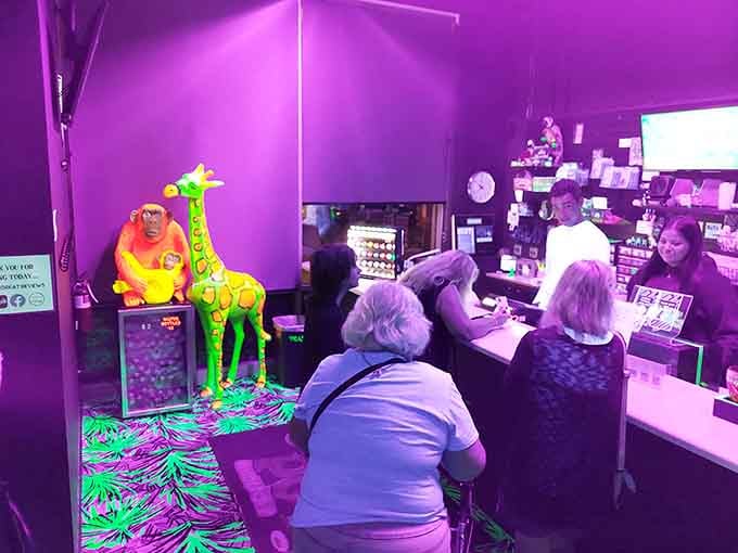The check-in area pulses with purple light, where friendly staff prepare visitors for their journey into the neon unknown.