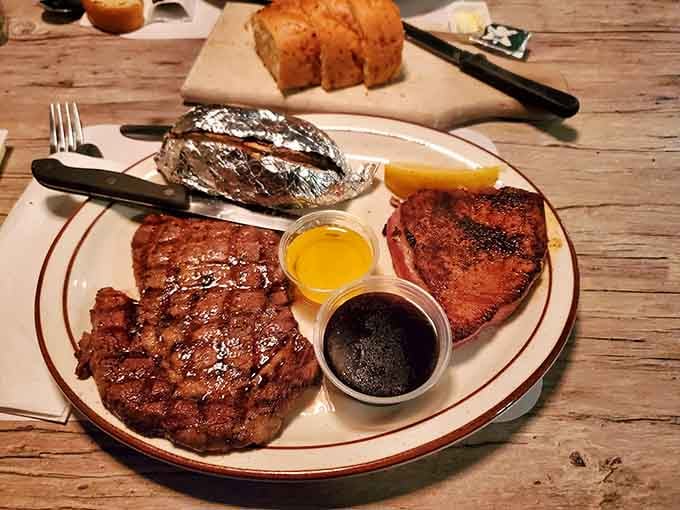 A carnivore's dream realized &ndash; perfectly grilled steaks share the spotlight with a baked potato in foil, all awaiting their destiny with melted butter and au jus.