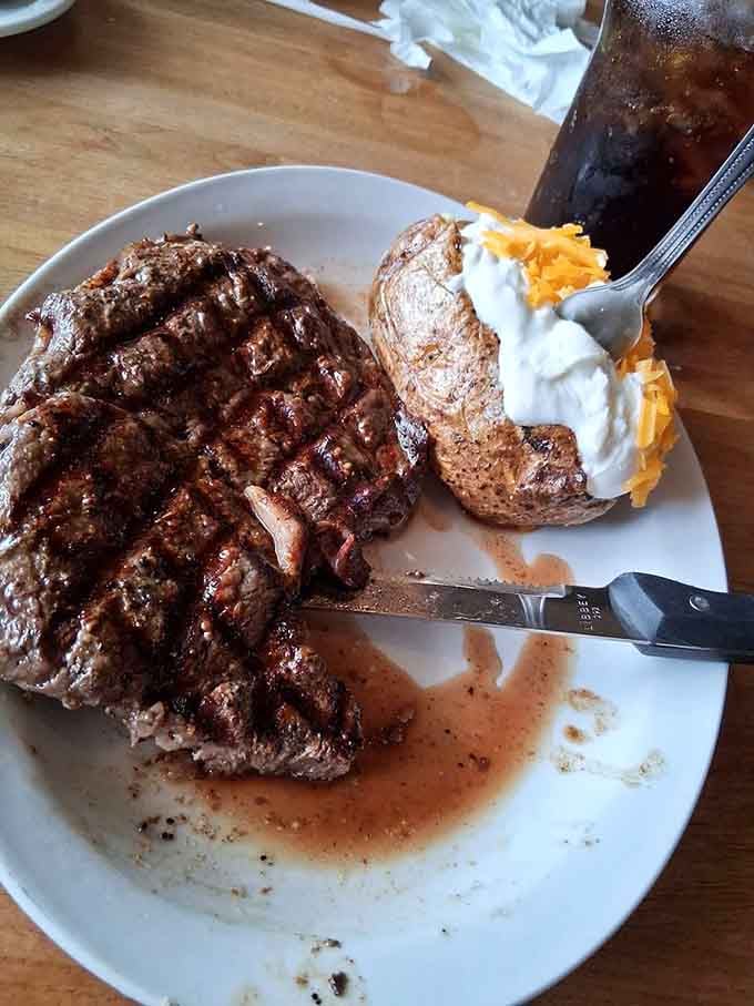 A perfectly grilled ribeye that would make Ron Swanson weep tears of joy, accompanied by a loaded baked potato worthy of its own fan club.