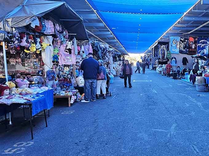 Blue tarps overhead create dramatic shadows while vendors display everything from toys to household essentials below.