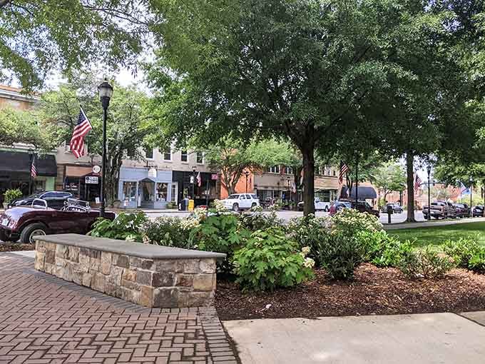 Mature oaks provide natural air conditioning over brick planters where someone actually tends the flowers with care.