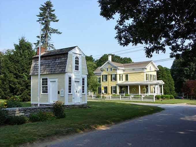 A tiny building stands beside a grand yellow house, proving that good neighbors come in all sizes and styles.