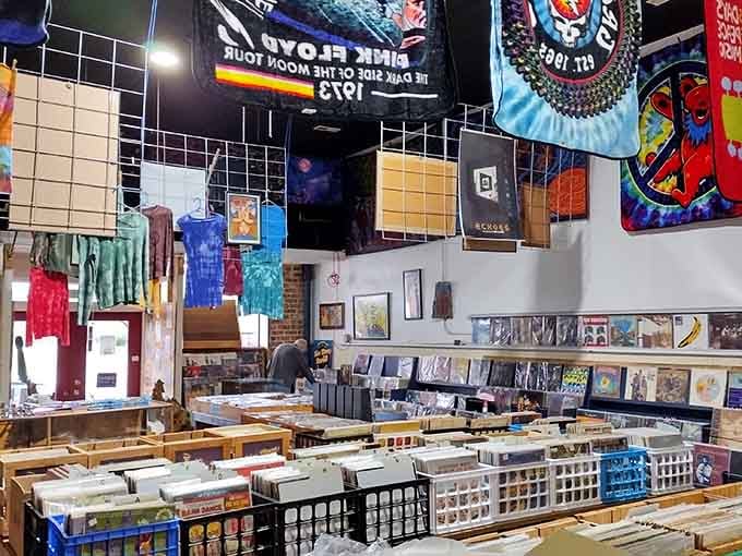 Tie-dye shirts hanging above endless record bins create a kaleidoscope of music culture, past and present colliding joyfully.