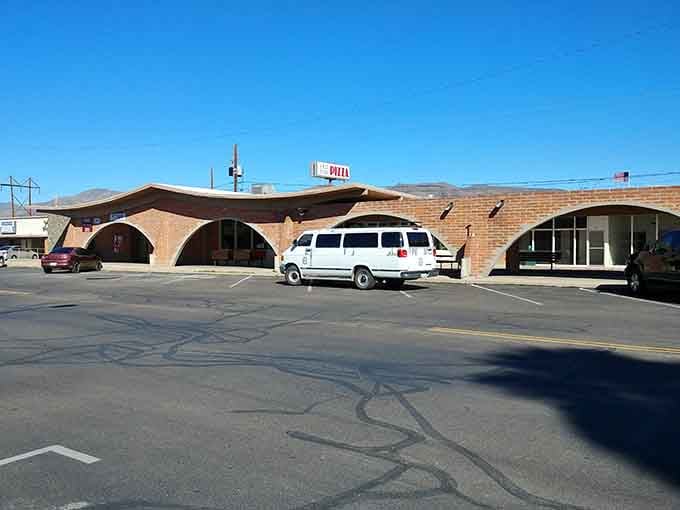 The sun casts long shadows across Old Time Pizza's parking lot, highlighting its unique brick arches. Pizza worth the desert drive!