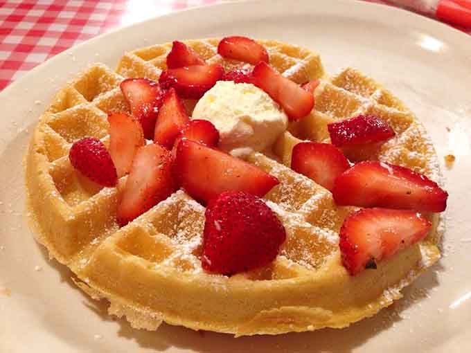Fresh strawberries piled on a waffle that's basically edible art, dusted with enough powdered sugar to make it snow.