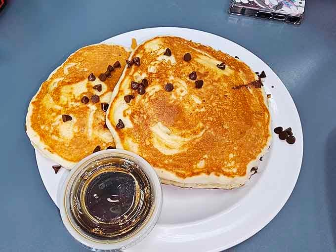 Chocolate chip pancakes that make you question why anyone would ever eat cereal again. The maple syrup cup stands ready for its grand moment.