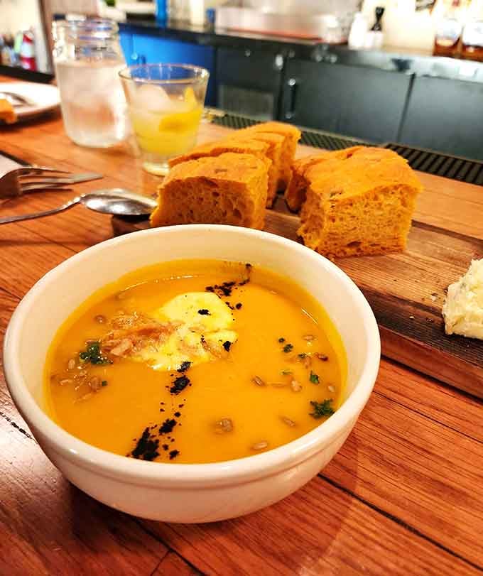 Vibrant squash soup that tastes like autumn decided to become liquid sunshine, served with bread for proper sopping purposes.