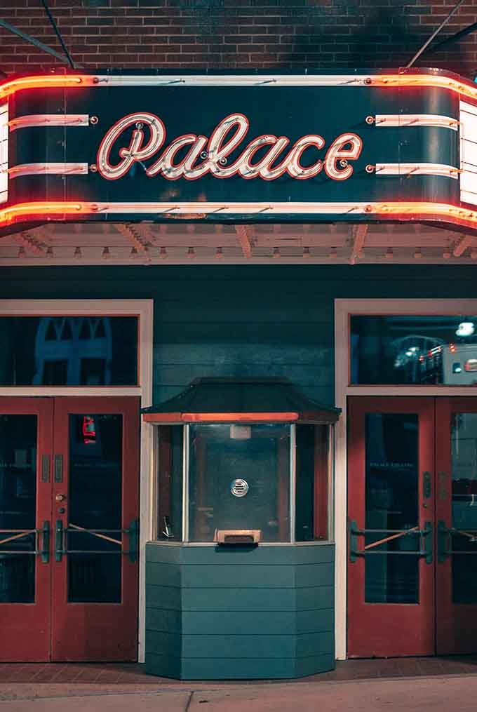 The Palace Theatre's vintage neon sign beckons like a beacon of affordable culture in a world of expensive entertainment.