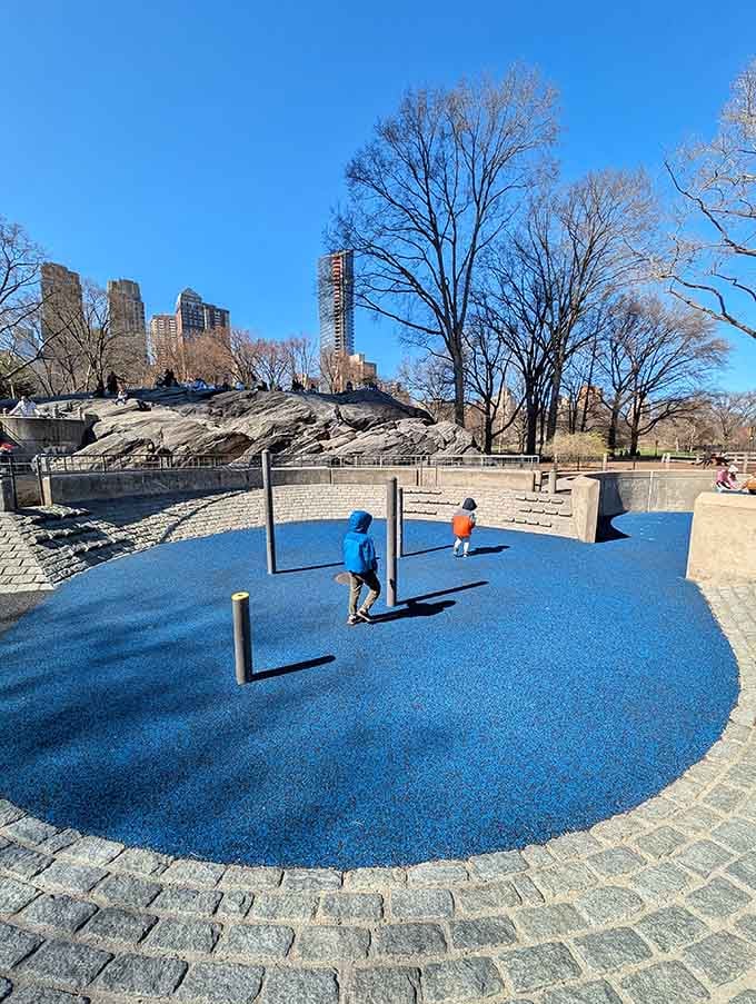 Blue safety surfacing meets creative play equipment, where kids navigate obstacles like tiny American Ninja Warriors in training.