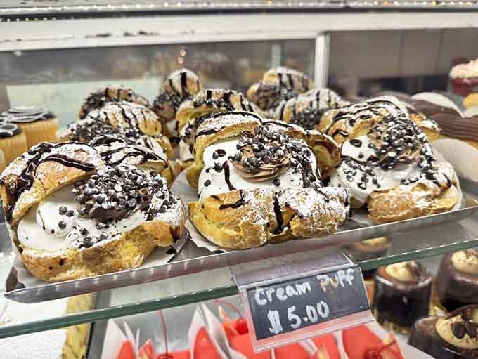 Cream puffs drizzled with chocolate in the display case, patiently waiting to become someone's very good decision today.