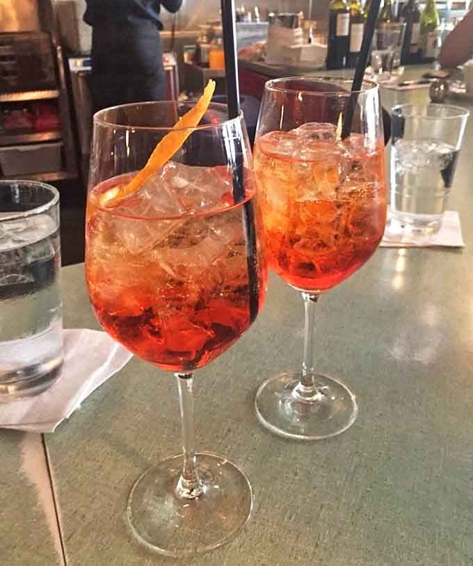 Those Aperol spritzes look like liquid sunshine decided to take a vacation in your glass and brought friends.