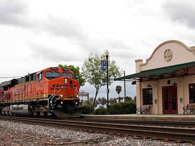 A freight train rumbles past the Spanish-style depot, connecting this small town to the wider world beyond the fields.