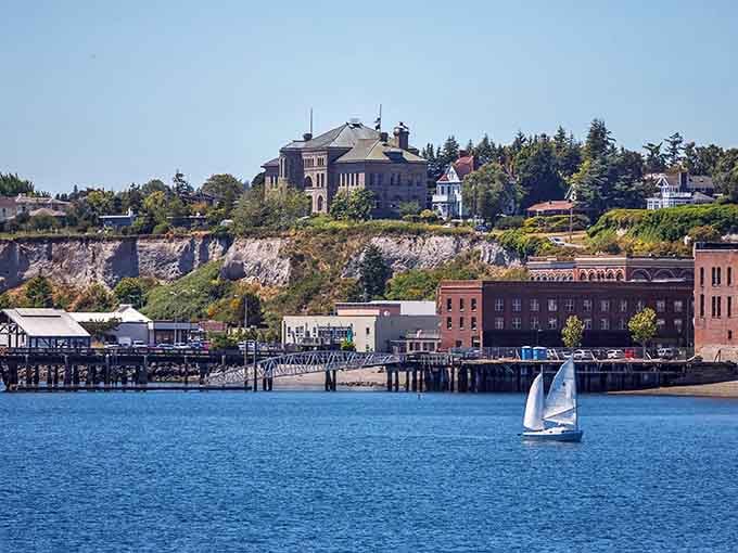 Ornate brick buildings line the waterfront while a lone sailboat glides past, connecting past and present in one perfect frame.