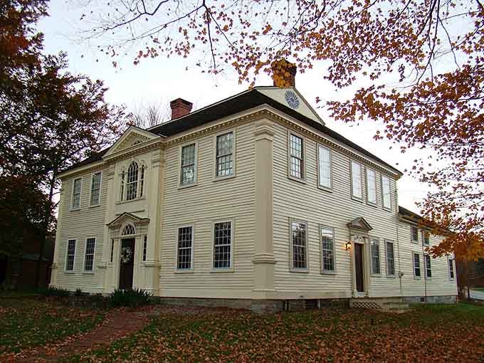 Autumn leaves frame this elegant colonial building where symmetrical windows and classic proportions define timeless New England beauty perfectly.