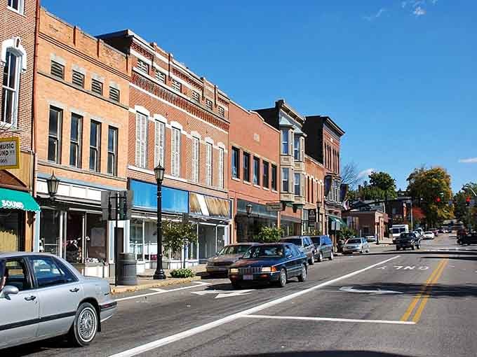 Brick buildings bask in afternoon sunshine, their windows reflecting blue sky while shoppers browse the sidewalk displays below.