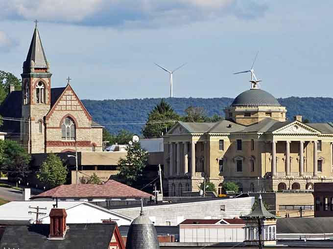 Church steeples and civic buildings rise against mountain backdrops, creating layers of history beneath modern wind turbines.