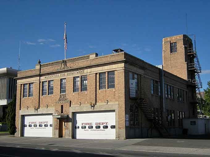 The vintage fire station stands ready with classic garage doors, representing small-town America when communities rallied together during emergencies.