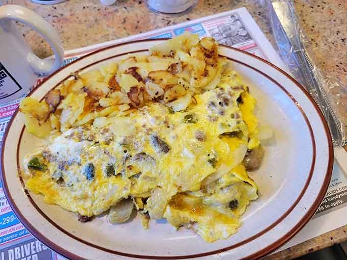 Fluffy omelet stuffed with vegetables and melted cheese, accompanied by crispy home fries that crunch with every satisfying bite.