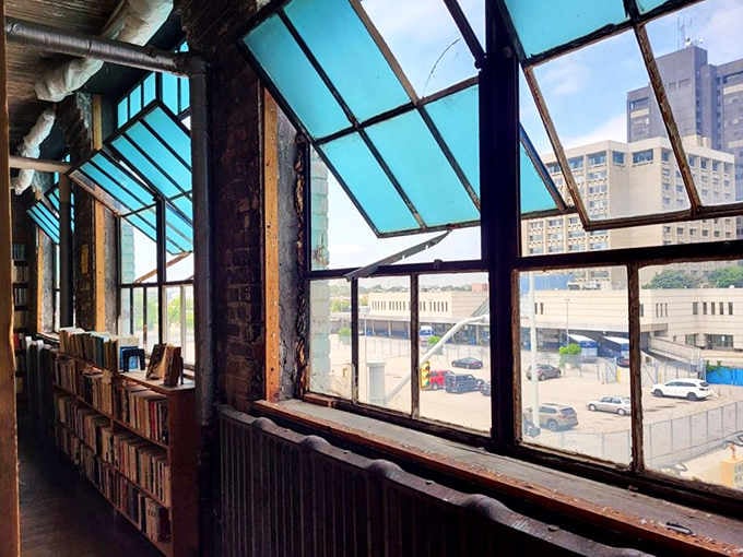 Natural light floods through industrial windows, offering readers a moment to pause and appreciate the cityscape beyond the books.