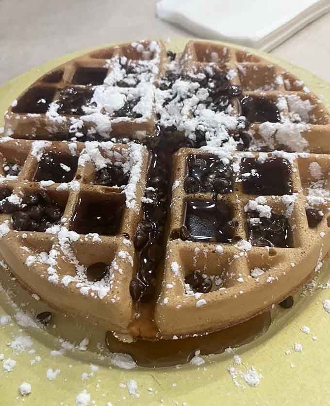 A Belgian waffle wearing powdered sugar like it's going to a fancy breakfast ball, syrup pooling in every square.