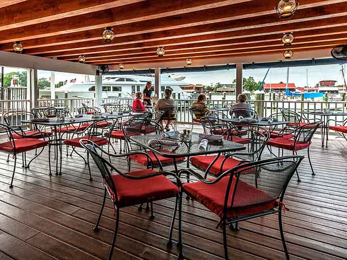 Waterfront dining with red chairs beckons like a siren song you actually want to answer.