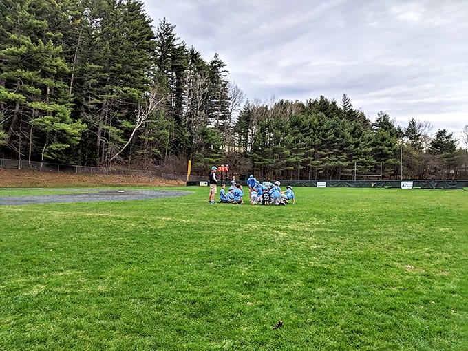 A quintessential New England sports moment: young athletes huddled on green fields, framed by towering pines and crisp mountain air.
