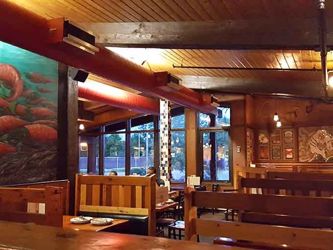 Wooden booths and warm lighting create the cozy ambiance that makes you linger long after your pizza is gone. That salmon mural? Pure Alaska.