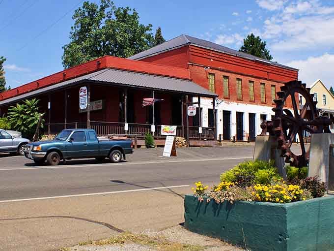 The old brick building with its water wheel decoration celebrates logging heritage while flowers add cheerful color below.