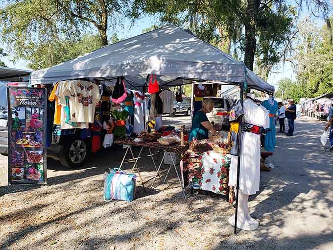 Colorful clothing and handmade crafts dangle from a cheerful tent where every purchase supports local artisans directly.