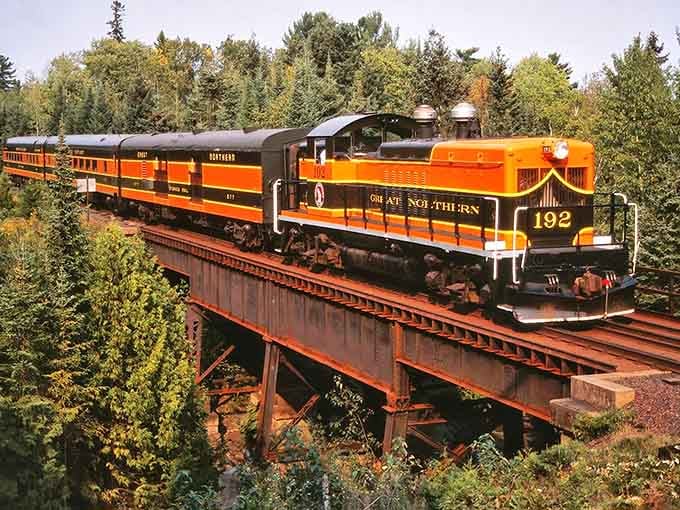 That distinctive orange and black paint scheme isn't just for show, it's a rolling piece of Minnesota history chugging across a trestle bridge.