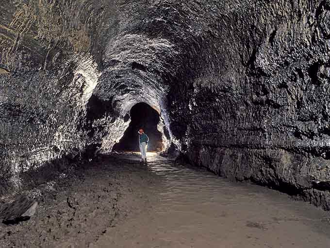 A lone explorer ventures deeper into the tube, their silhouette dwarfed by walls that once channeled rivers of fire.
