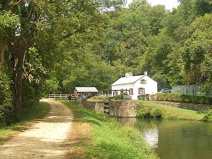 A quiet canal-side cottage nestled among lush trees offers a peaceful escape along a scenic walking path.