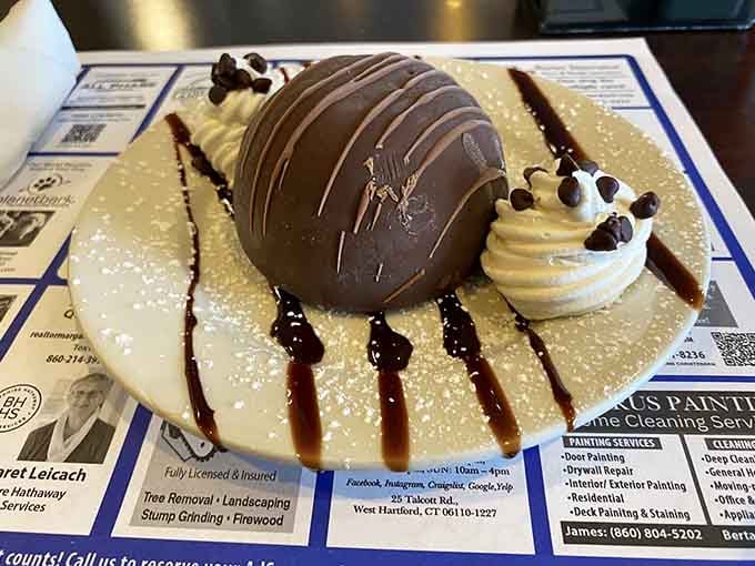 The Chocolate Dome Bombe looks like edible architecture, decorated with precision and probably containing enough chocolate to solve problems.