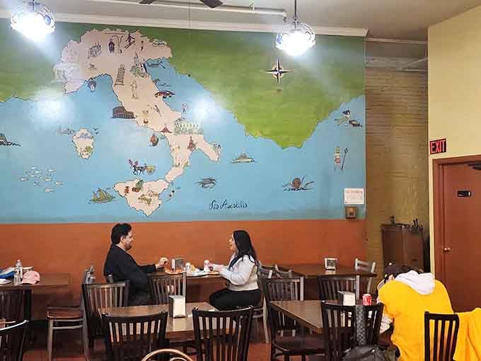 Diners enjoying their meals beneath that cheerful Italy mural, living their best carb-loaded life right now.