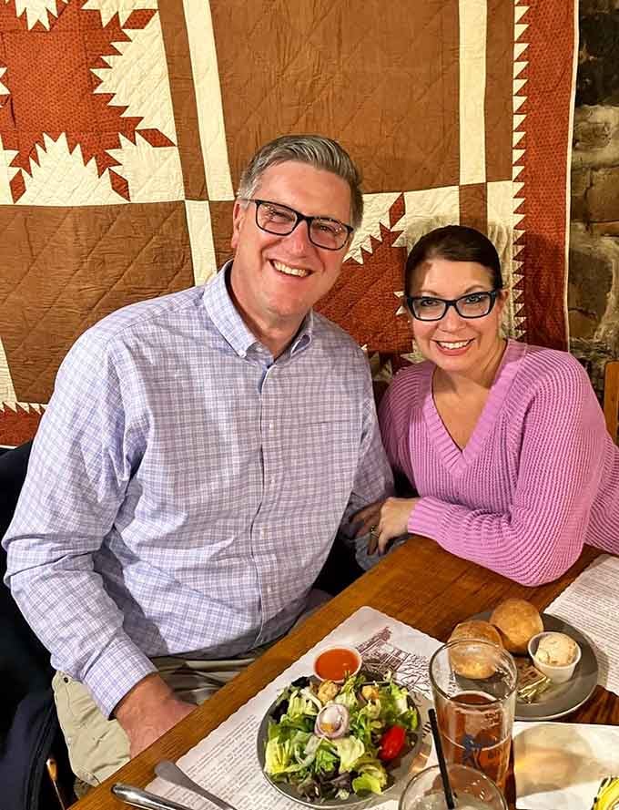 Happy diners enjoying their meal beneath a handmade quilt, where history and hospitality meet over good food together.