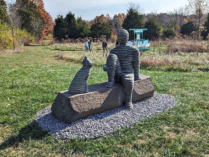 Three figures share a bench moment, their stacked metal forms suggesting conversation without saying a single word.