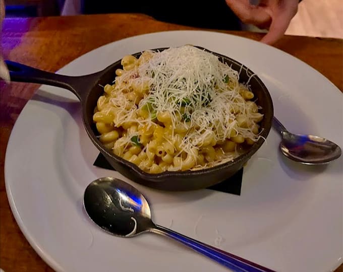 Mac and cheese served in a cast iron skillet with a mountain of shredded cheese on top.