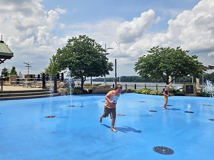 Kids running through water jets with the kind of pure joy that makes you remember summer actually matters.